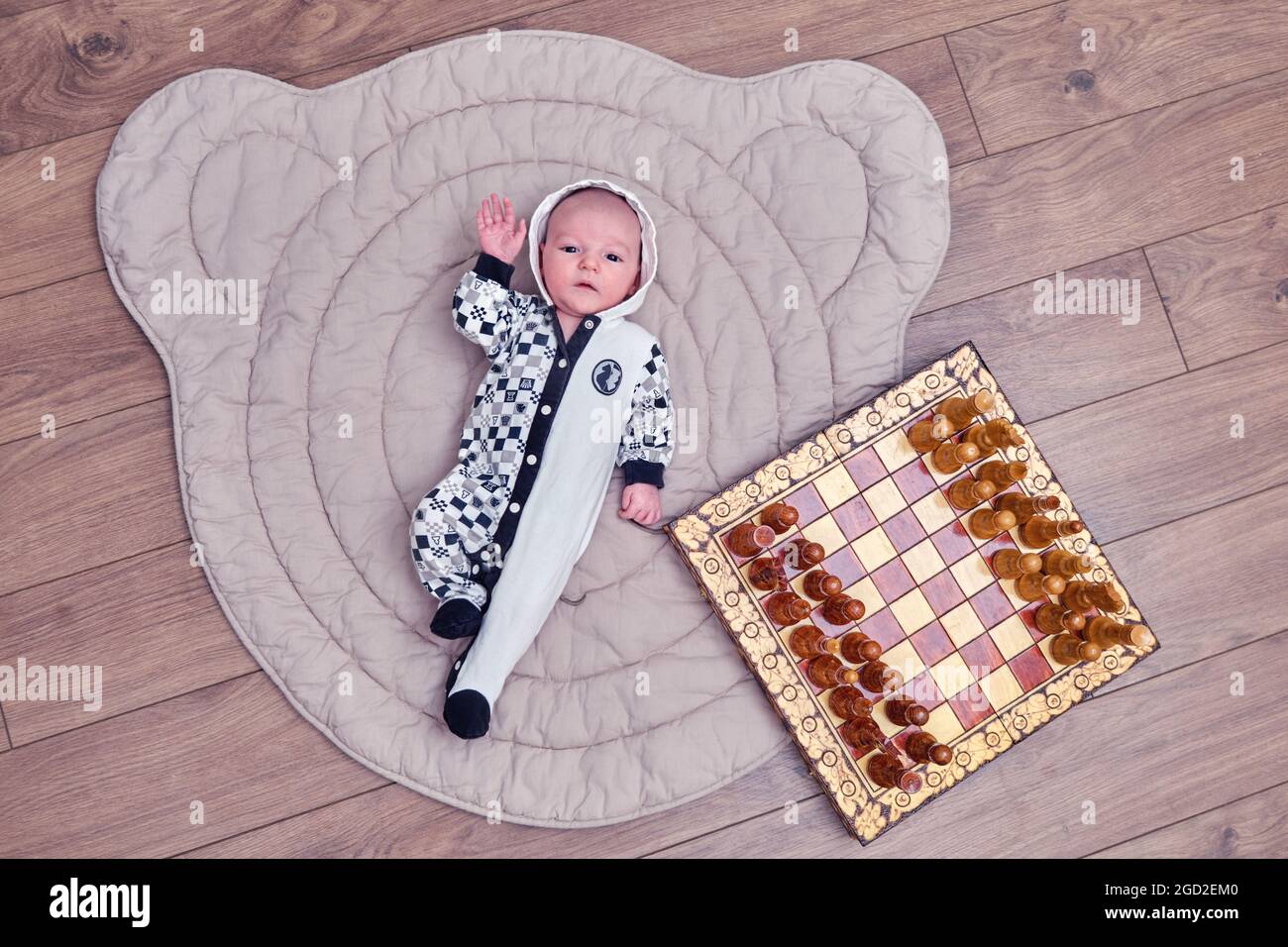 Newborn baby boy in a chess suit near a chessboard with placed pieces ...