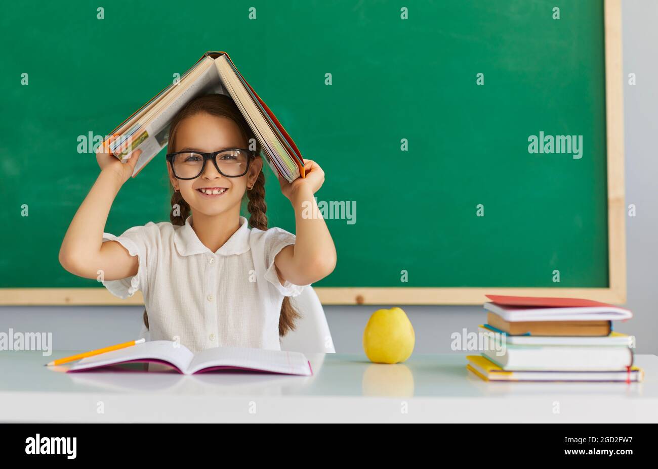 Schoolgirl in glasses holds a book over her head while sitting at a ...