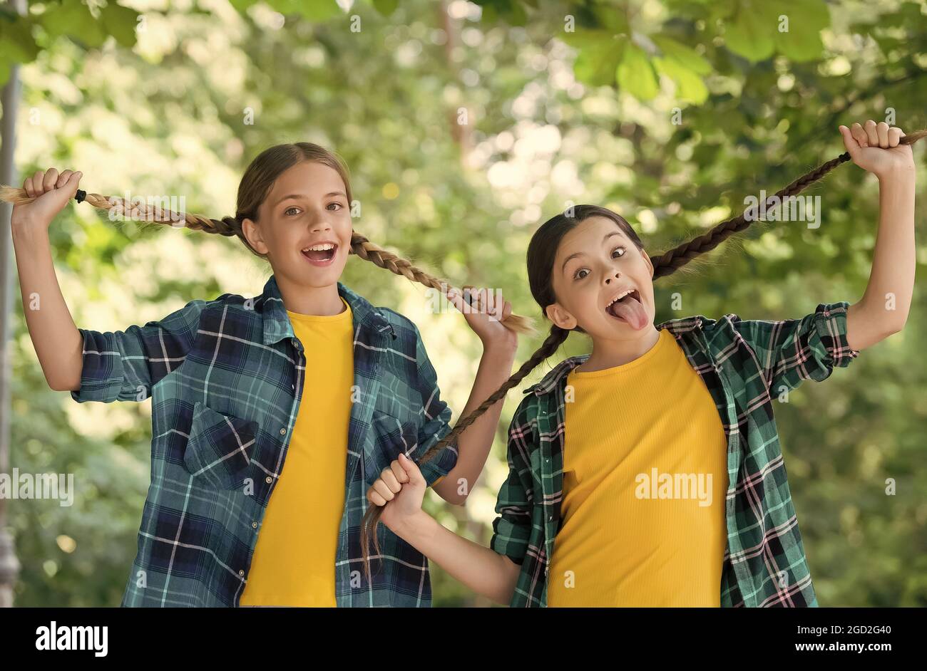 Funny children hold long hair plaits grimacing mouths in casual fashion ...