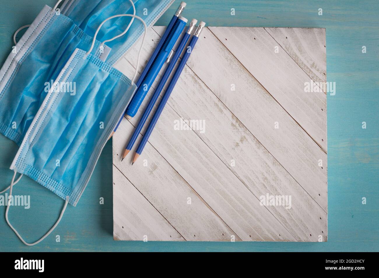 blue disposable face mask with pencils and eraser beside white wood ...