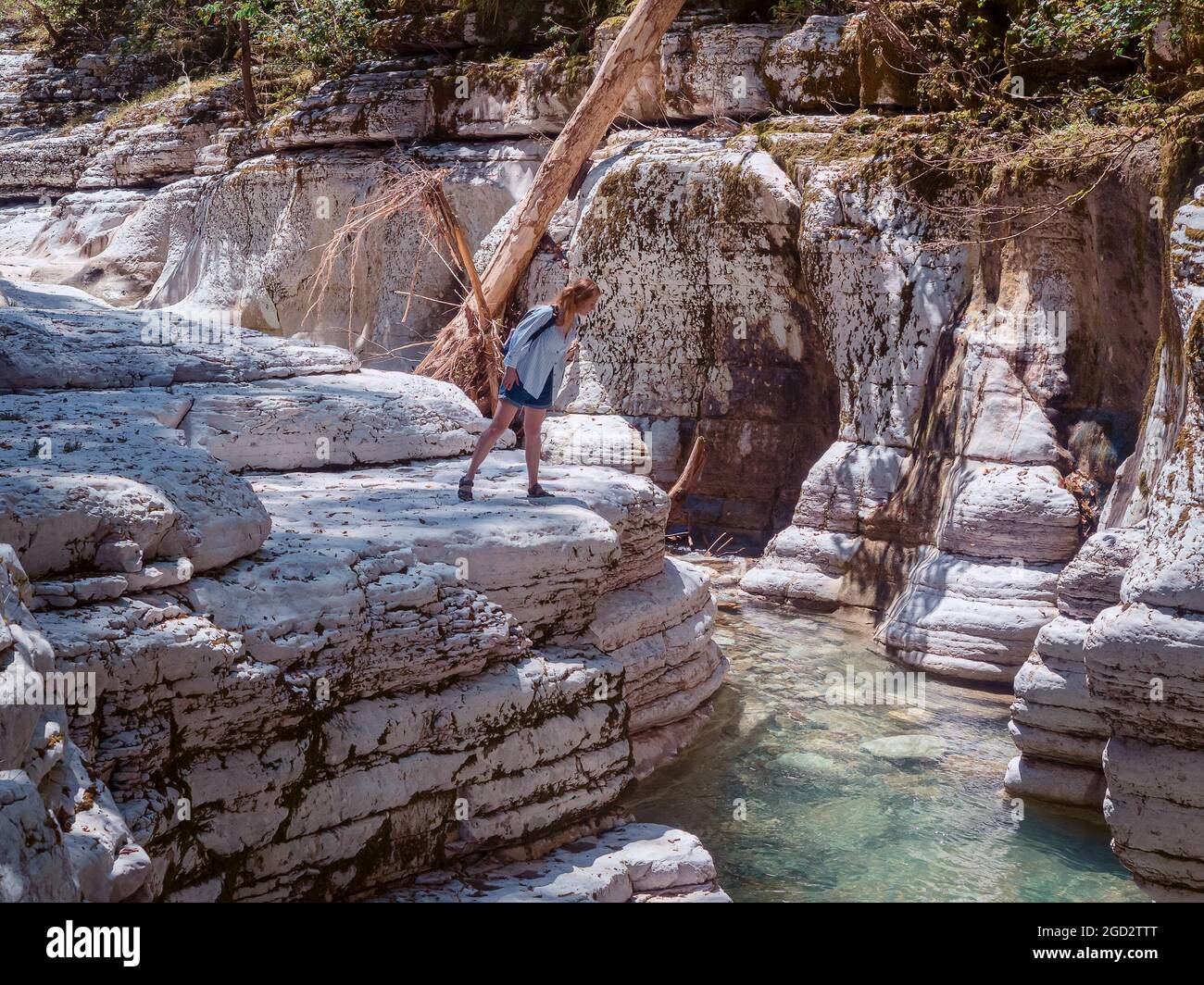 A girl stands on white canyon looking down into a clear river flowing ...