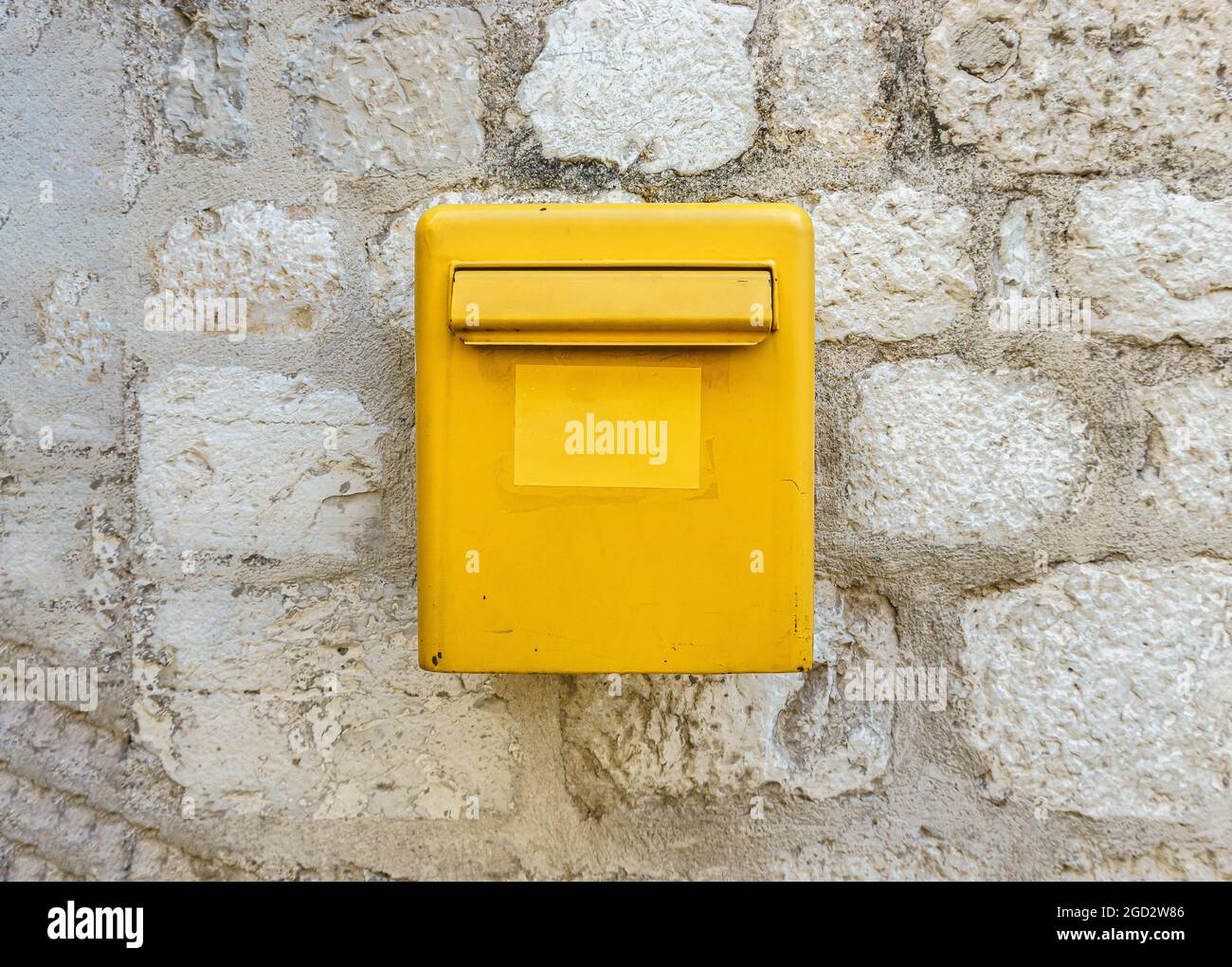 A yellow mailbox on a light stone wall. Box for letters and postcards ...