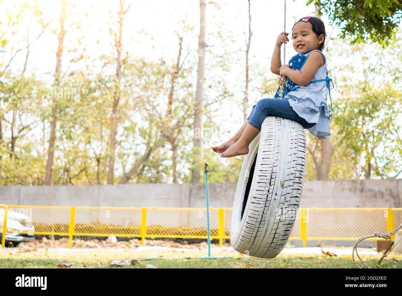 Little Thai girl hanging on a swinging car tires at a playground Stock ...