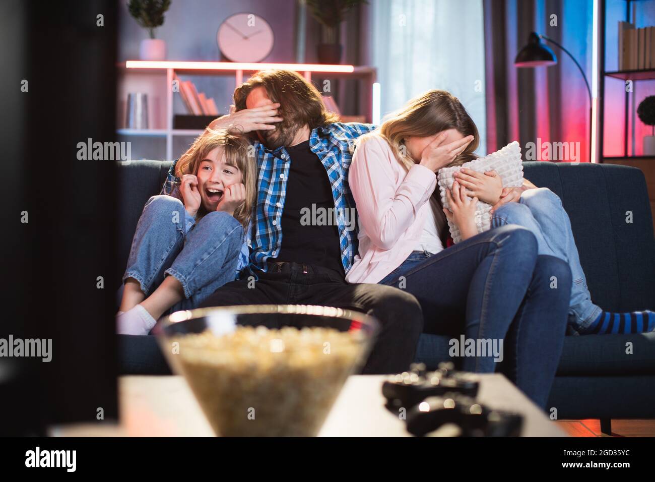 Scared parents with two kids hiding eyes while watching horror movie at ...