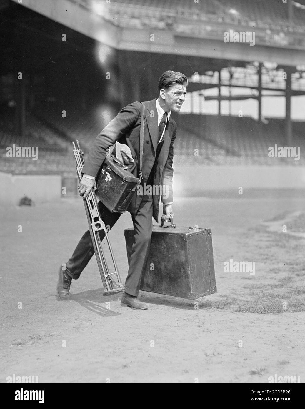 Man in suit carrying equipment cases in stadium ca. between 1909 and ...