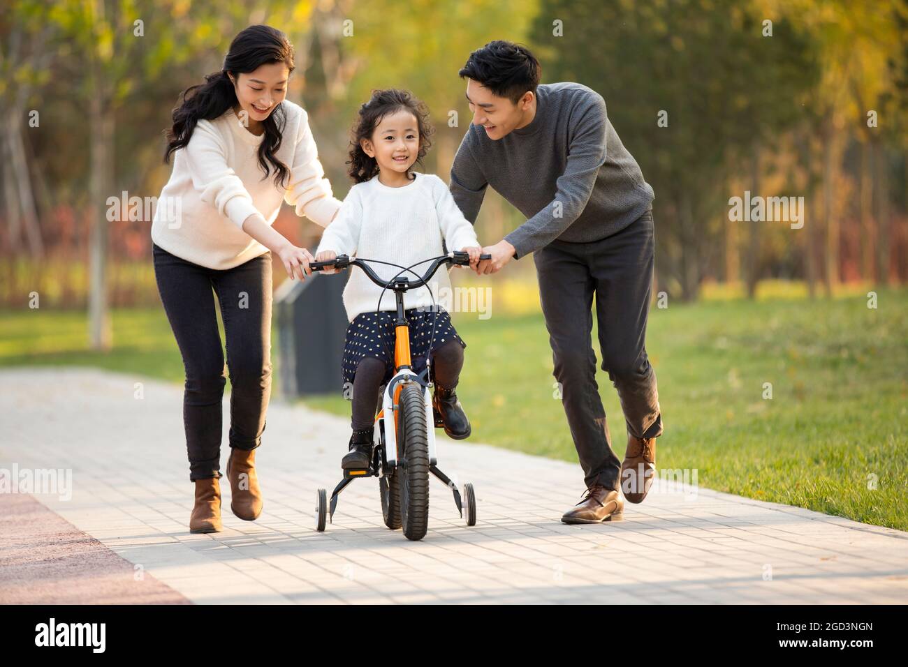 Parents teaching child how to ride bike Stock Photo - Alamy