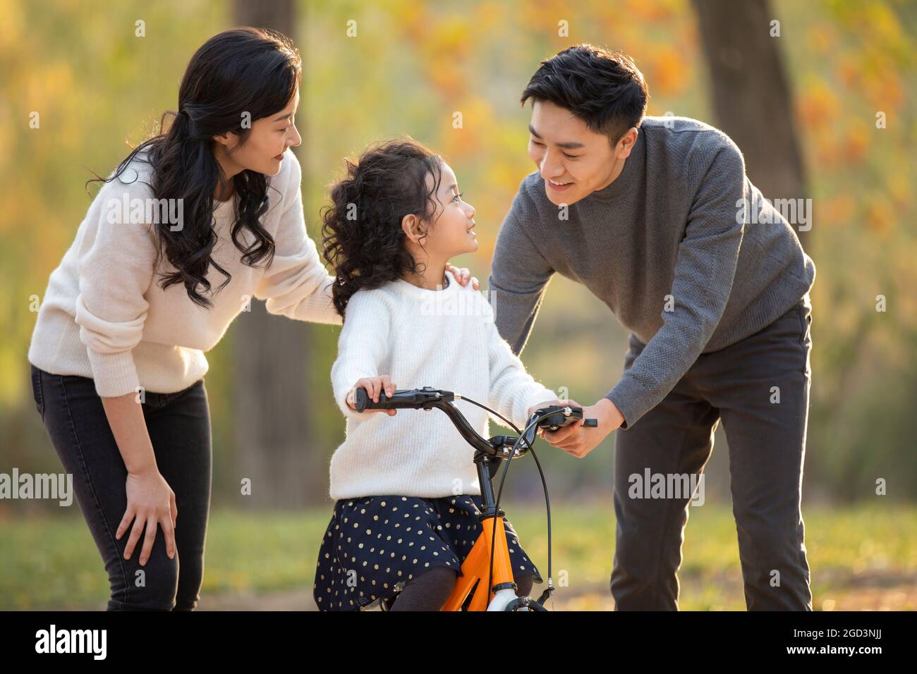 Parents teaching child how to ride bike Stock Photo - Alamy