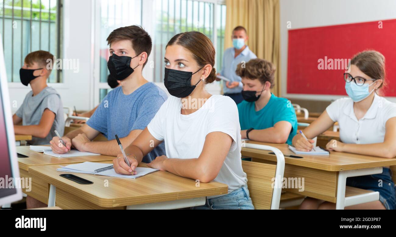 Teenage students in protective masks studying in classroom with teacher ...