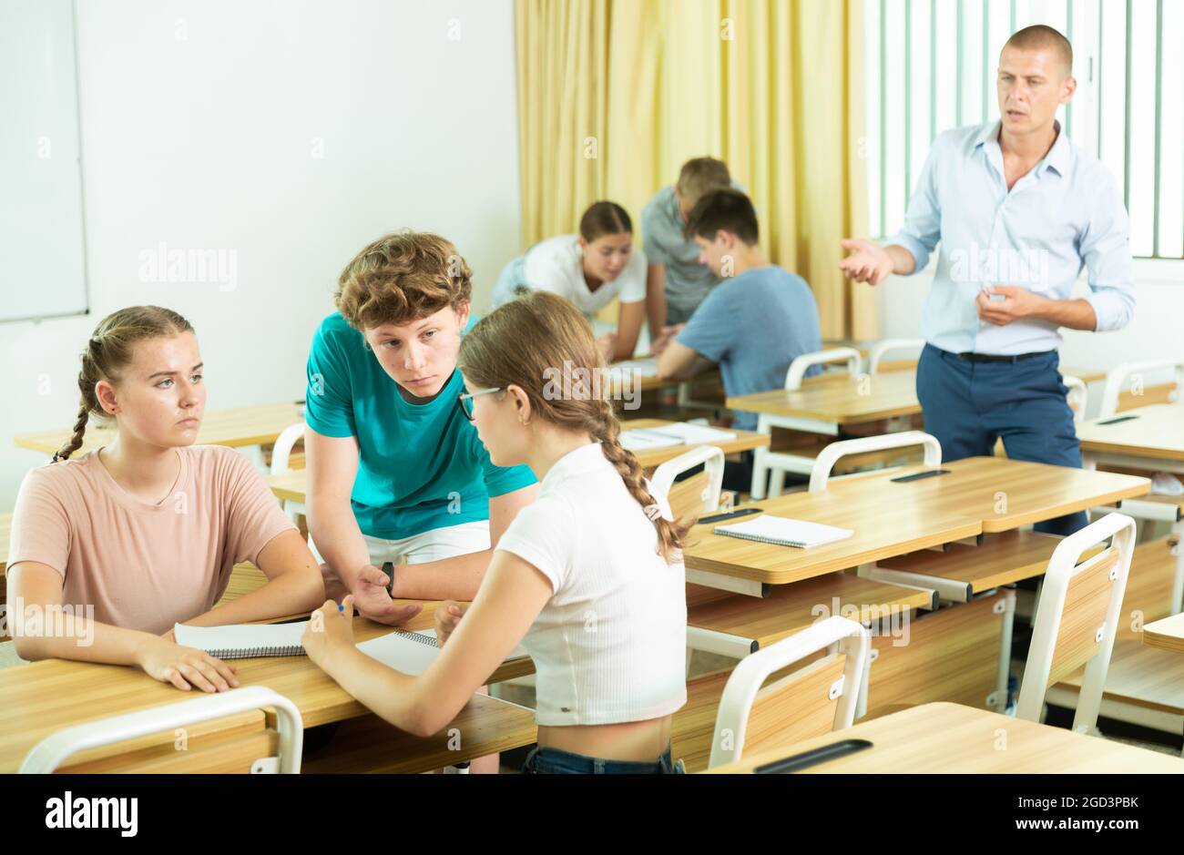 Teenage students discussing learning material in groups in classroom ...