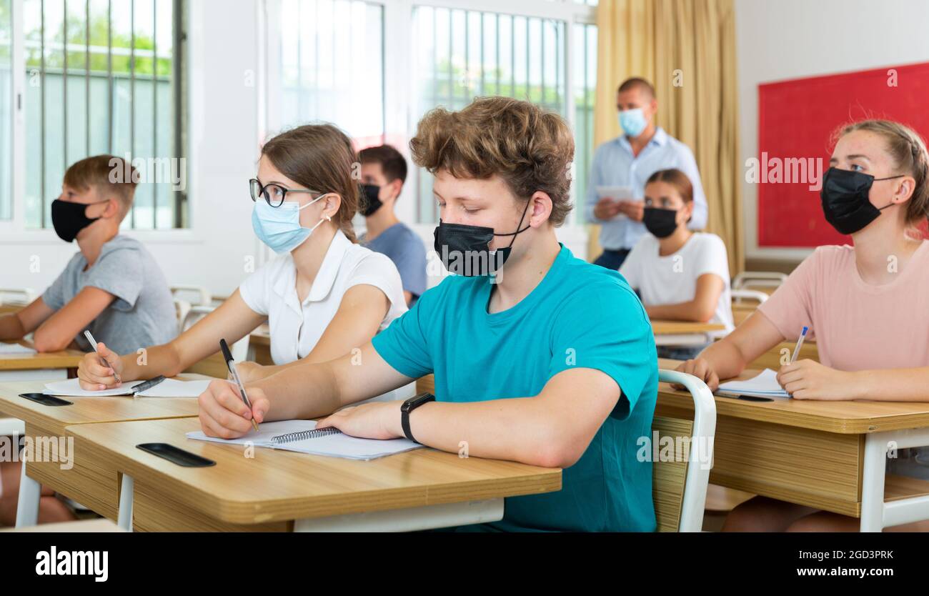 Teenage students in protective masks studying in classroom with teacher ...