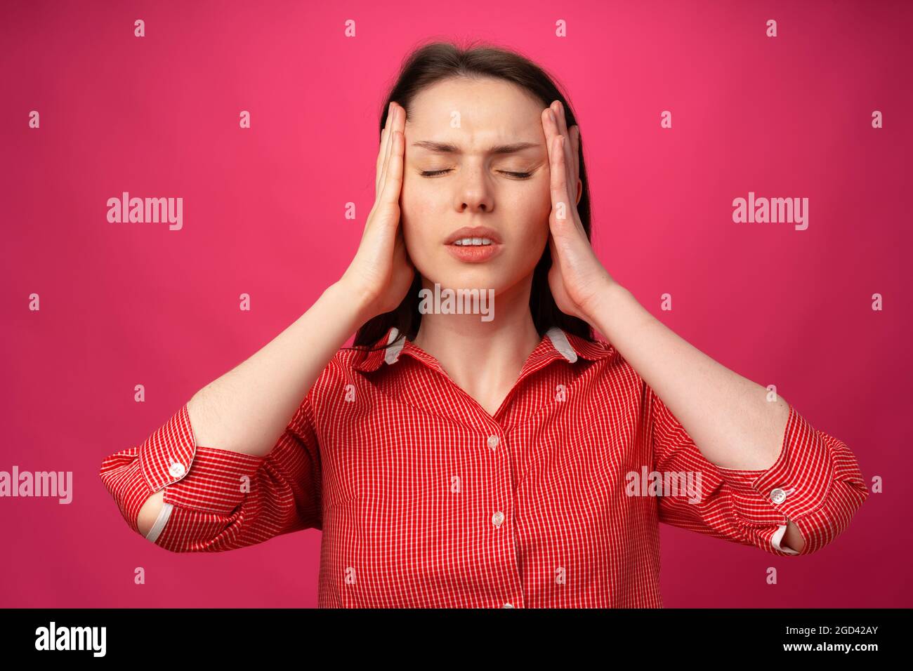 Young stressed woman with headache touching head against pink ...