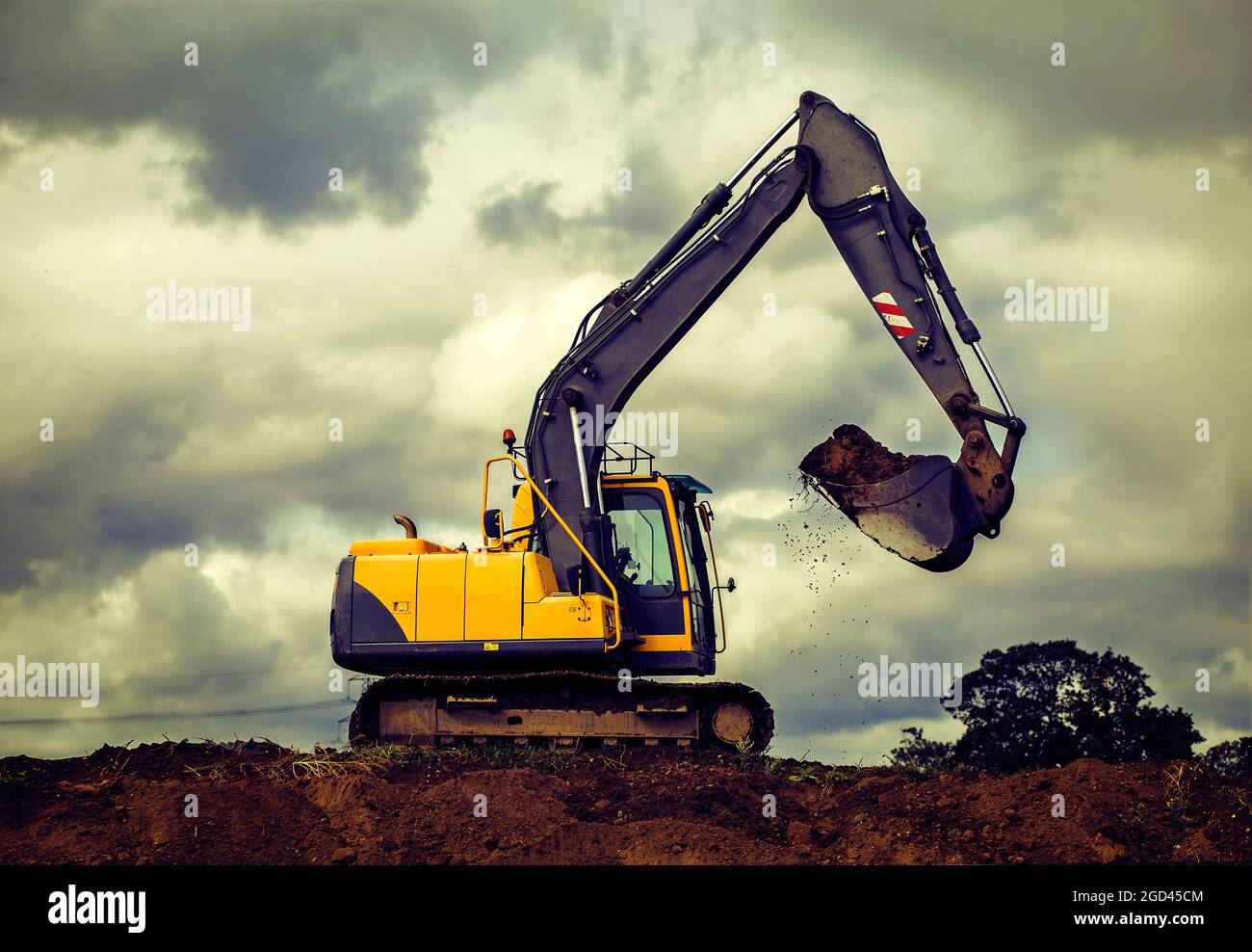 Yellow digger on hill lifting dirt against a dramatic cloudy sky Stock ...