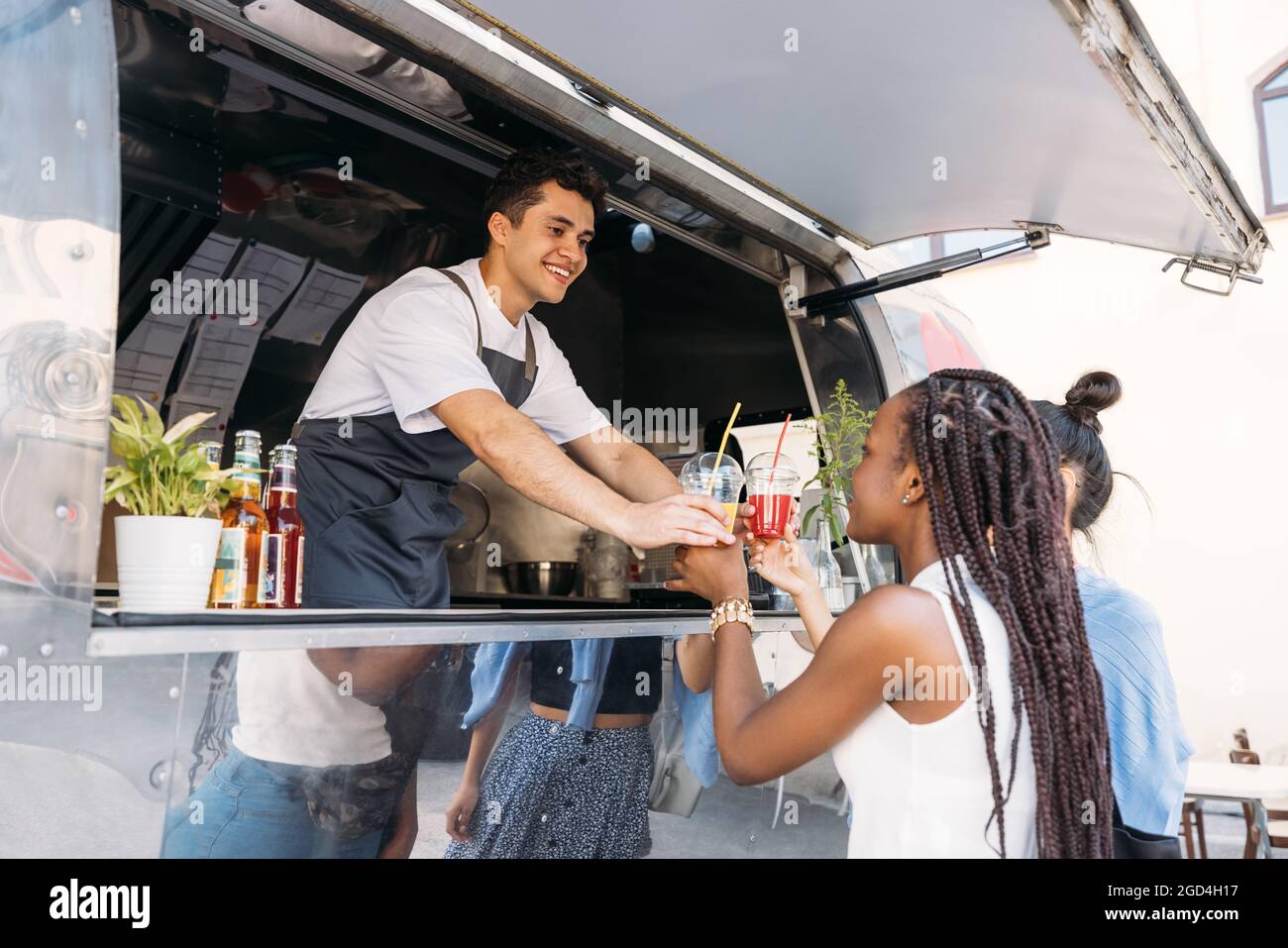 Two customers receiving drinks from food truck owner. Cheerful salesman ...