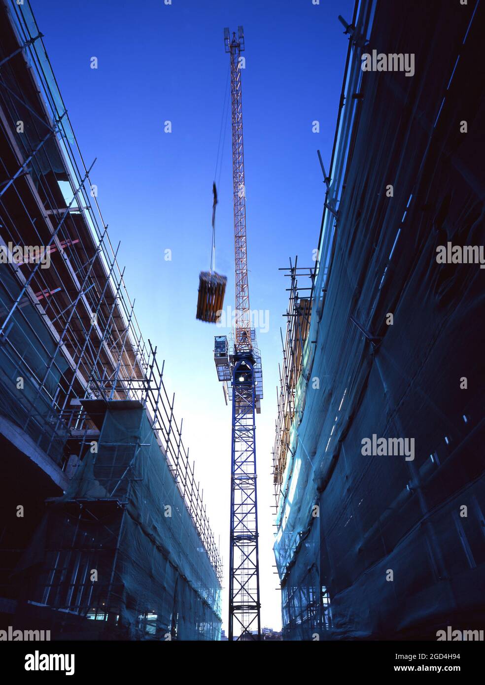 Looking up to a tower crane lifting building materials high into the ...