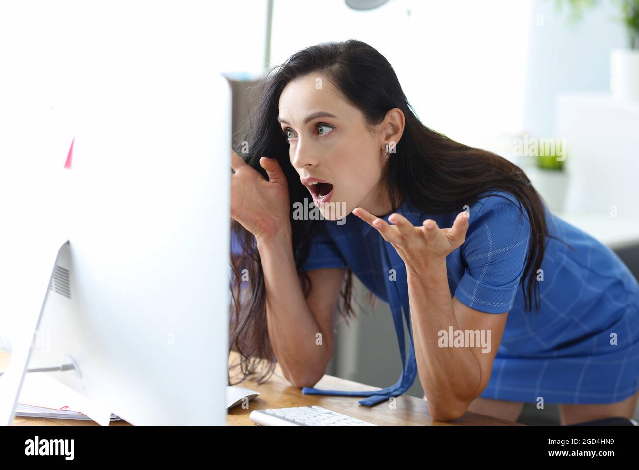 Shocked woman sits at table and looks at computer screen eyes widening ...