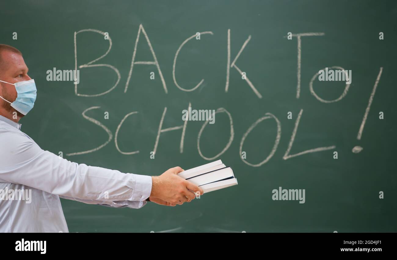 Teacher with face mask welcoming children back at school after lockdown ...