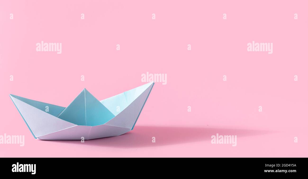 Folded paper origami blue ship with shadow on pink background with copy ...