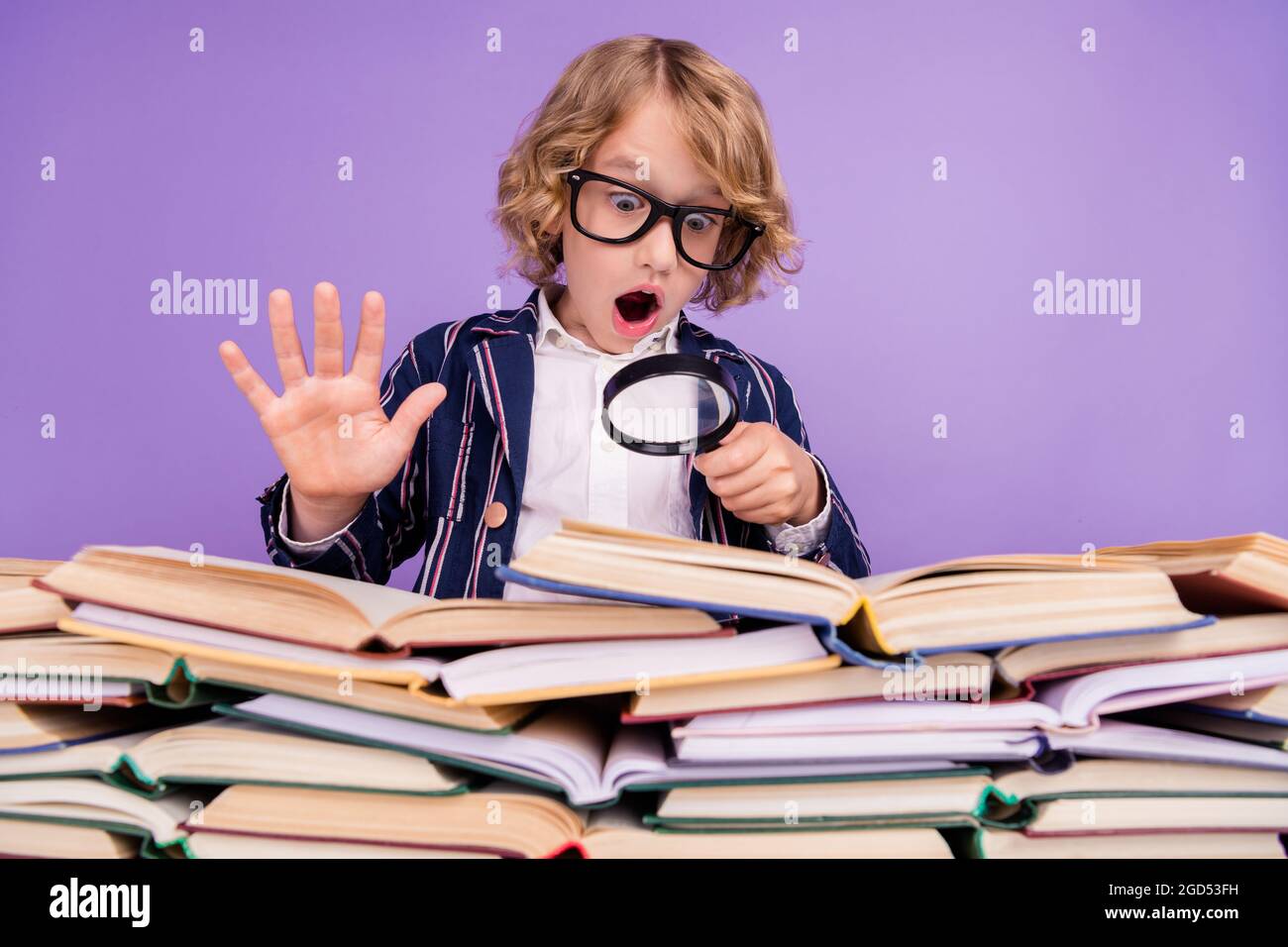 Portrait of trendy amazed schoolboy reading pile book using loop ...