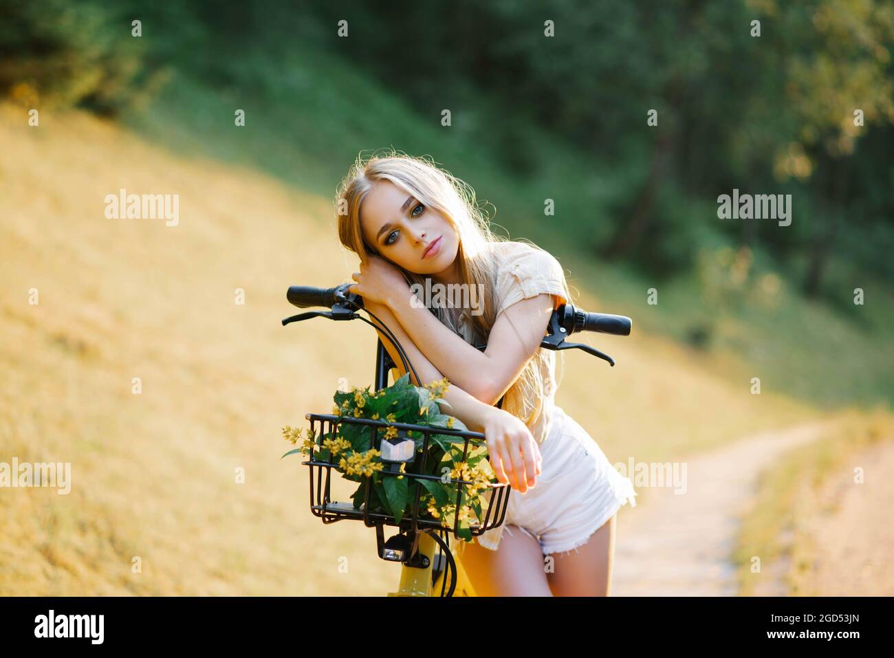 Portrait of a happy beautiful young girl with a bicycle and flowers on ...