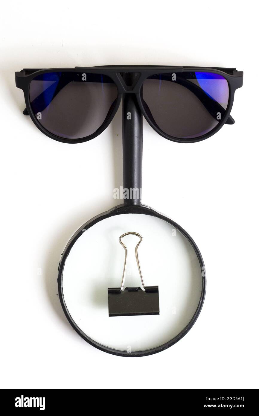 Magnifier, sunglasses and a clip on a white surface viewed from above ...