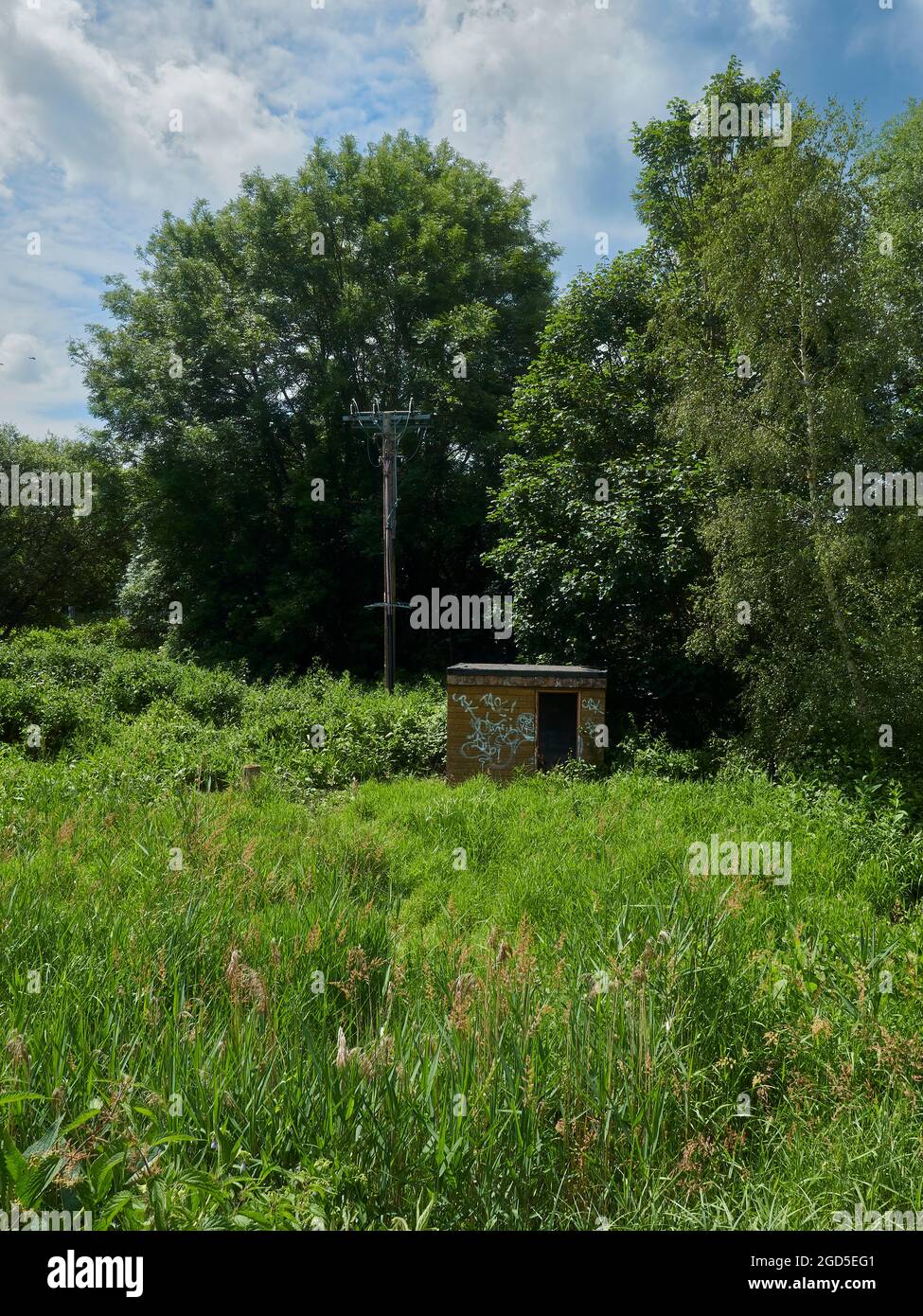An abandoned, graffiti scarred brick hut next to a telegraph pole, both ...