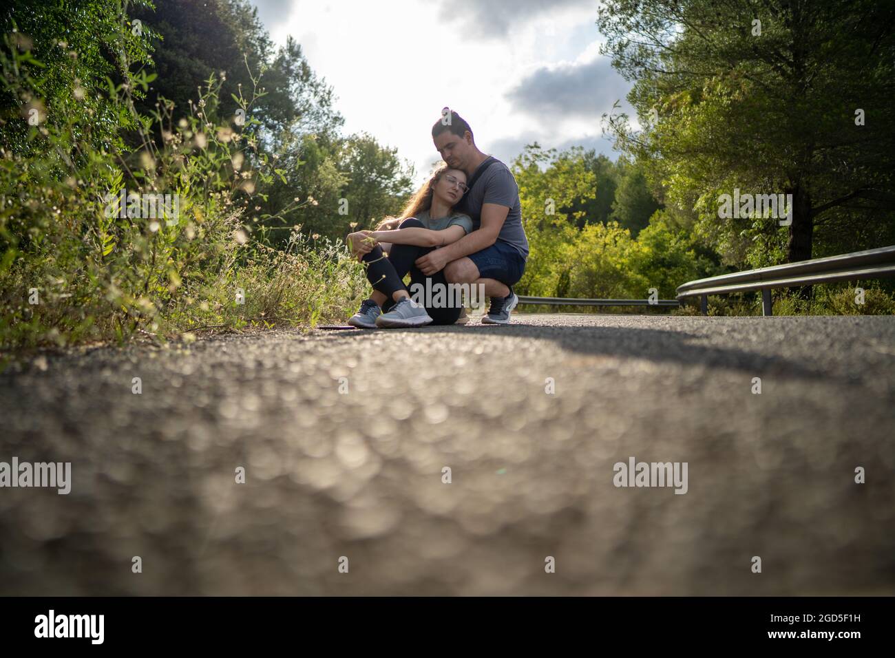 Young couple sitting on the ground hugging each other with trees on the ...