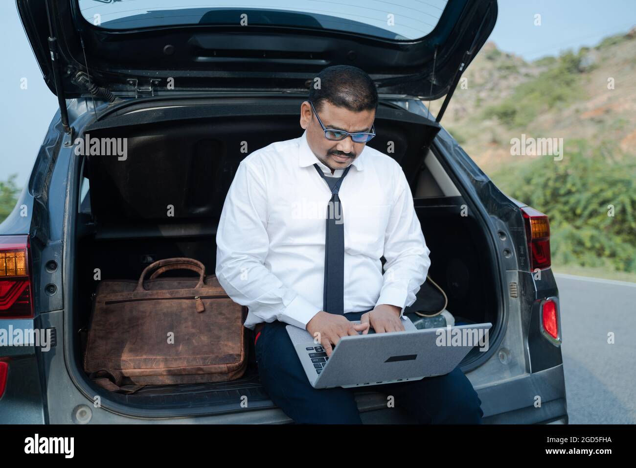 Young businessman working from the car trunk or boot near roadside ...