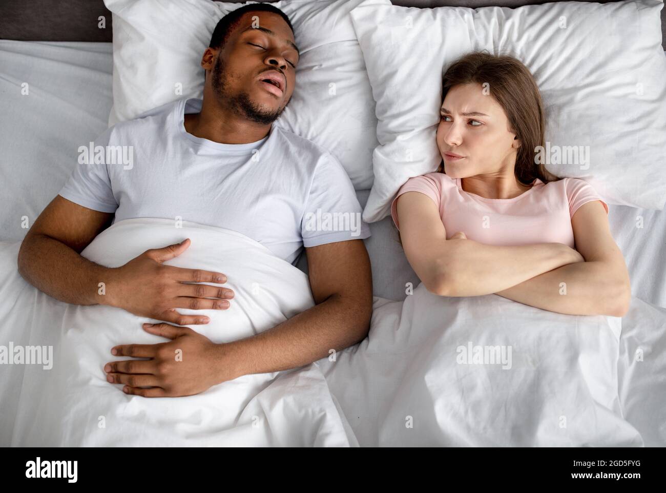 Top view of irritated young woman annoyed by her black husband snoring ...