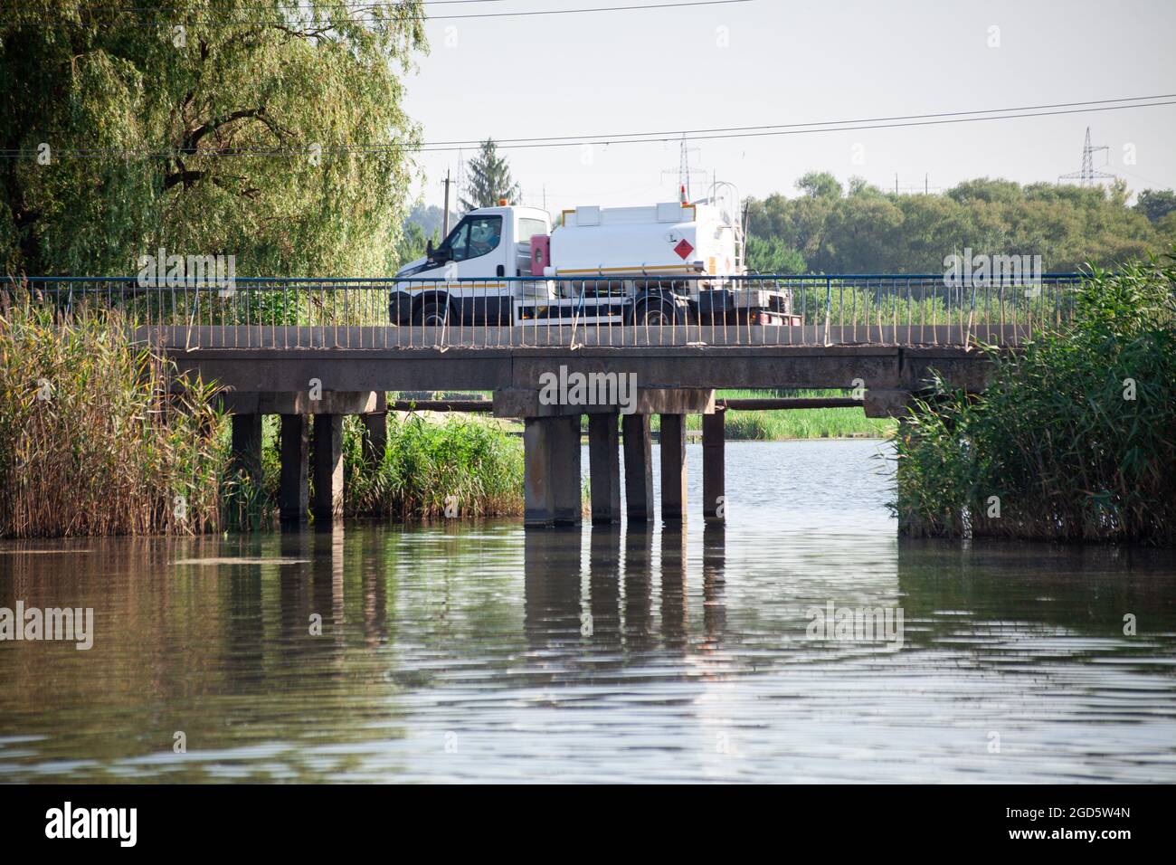 White tanker truck on concrete bridge over a small river with green ...