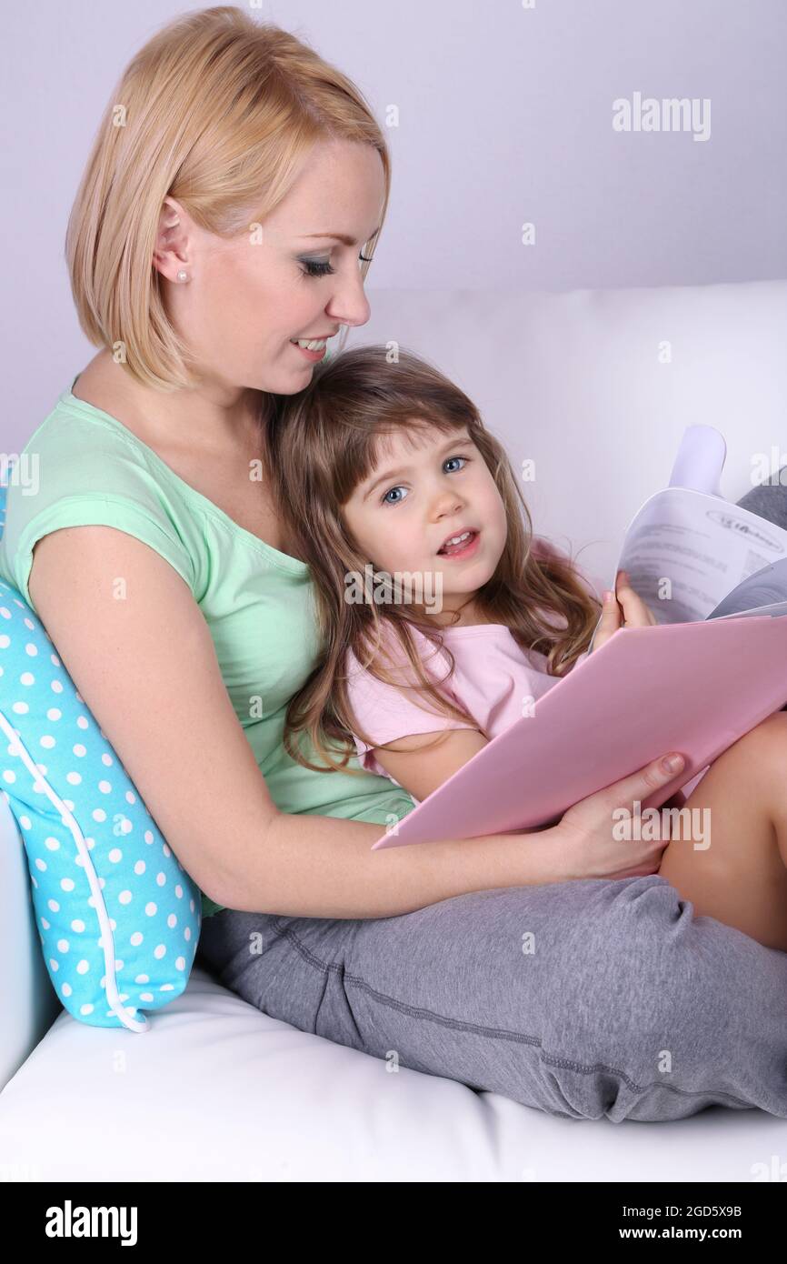 Pretty little girl reading book with mother on sofa on gray background ...