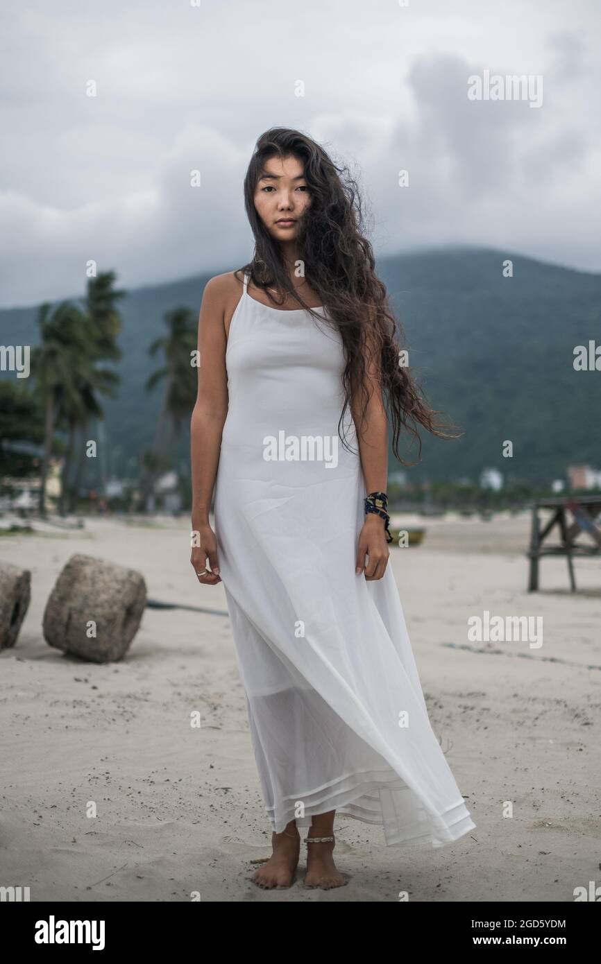 Peaceful young mongol woman in white dress walking on the beach ...