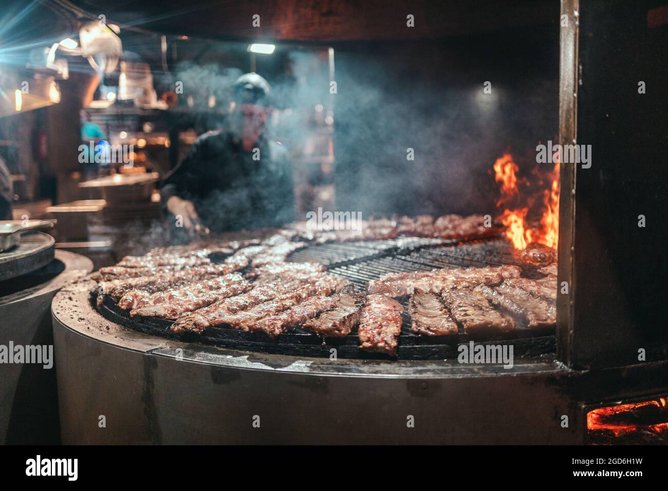 Professional chef grills pork or beef ribs on an open round grill oven ...