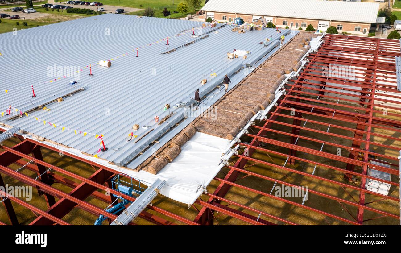 Construction workers installing insulation and roof panels on a large warehouse building from an ...