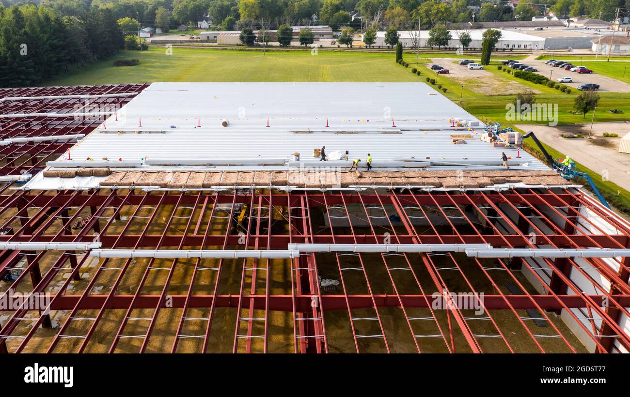 Construction workers installing insulation and roof panels on a large ...