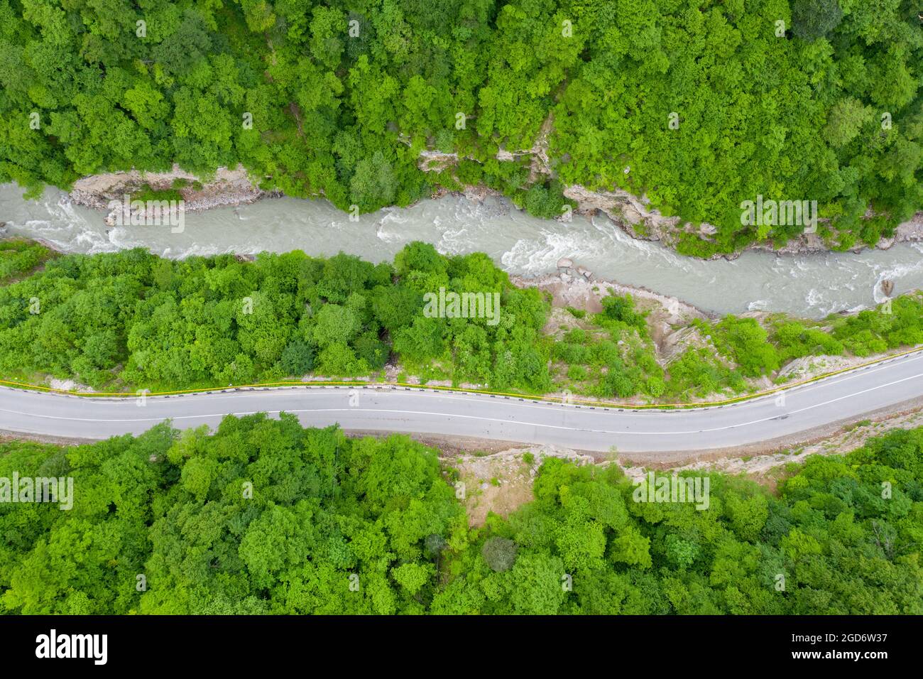 Aerial shot of a river flow route and parallel highway with green trees ...