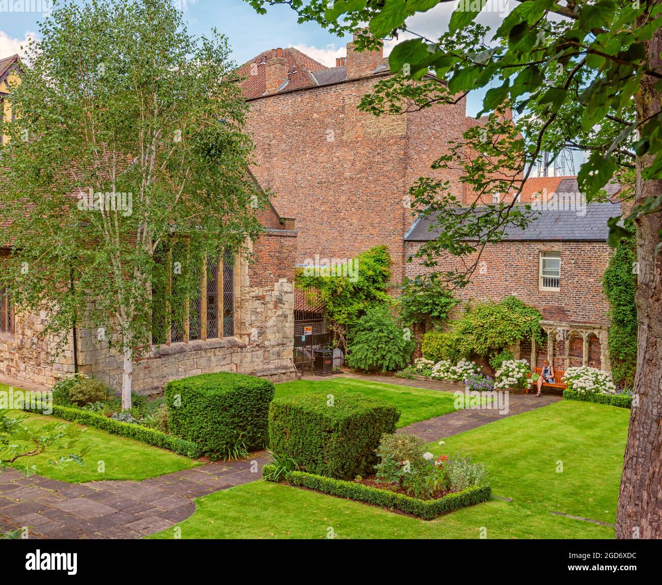 A small garden beside a medieval building. A bench is set against an ...