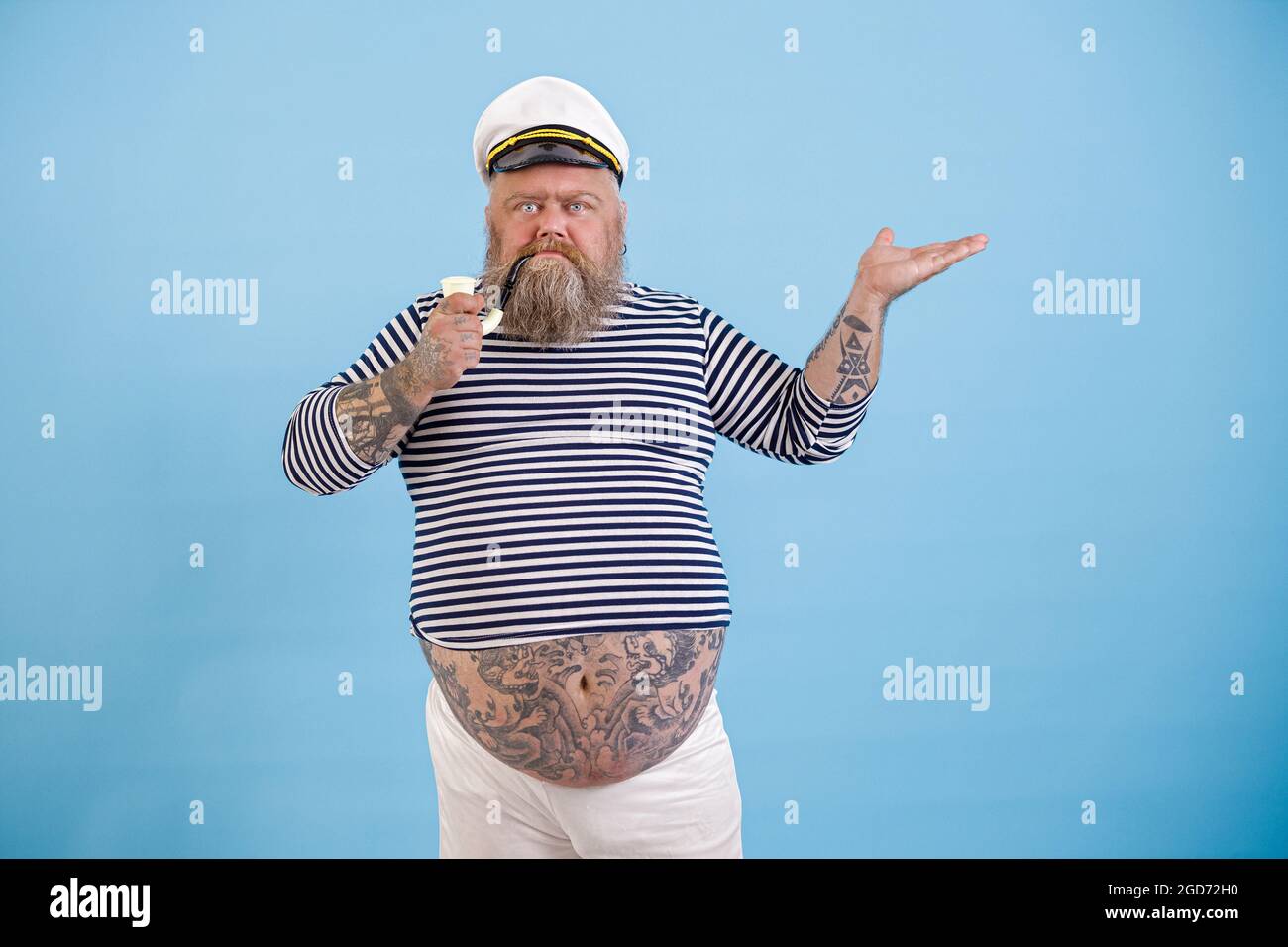 Dashing fat man with tattoos in sailor suit points aside on light blue ...