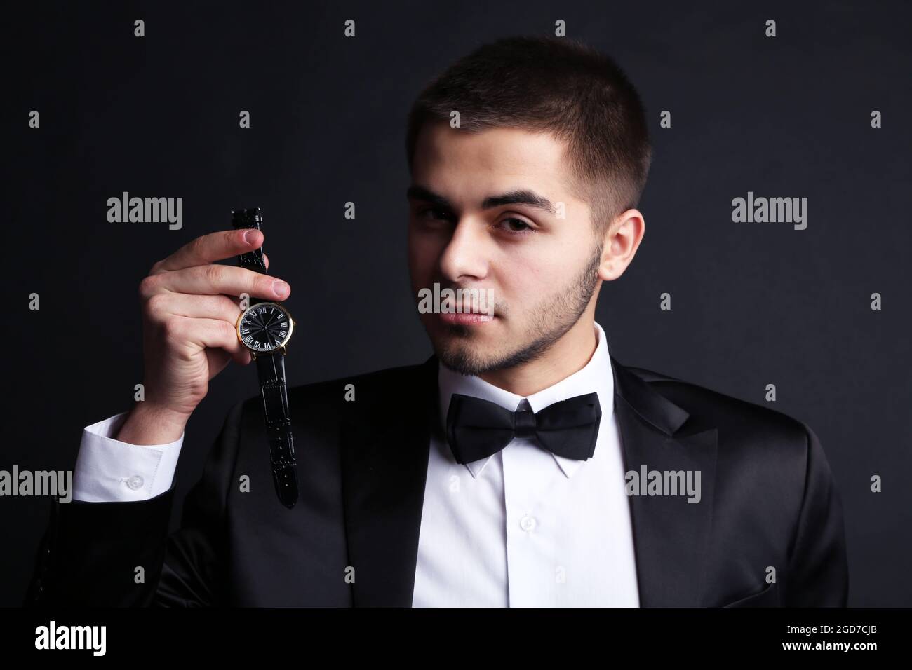 Handsome young man in suit holding watch on dark background Stock Photo ...