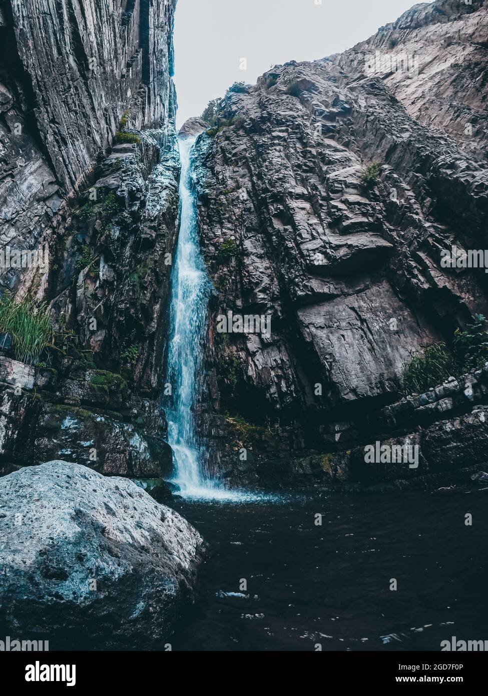 Vertical shot of a beautiful waterfall falling onto a small lake with ...
