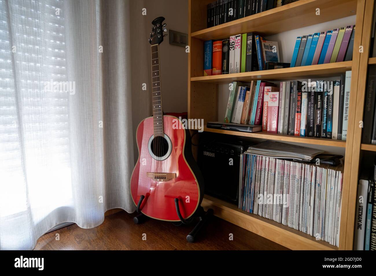 Red acoustic guitar on a stand at home, next to a bookcase full of ...