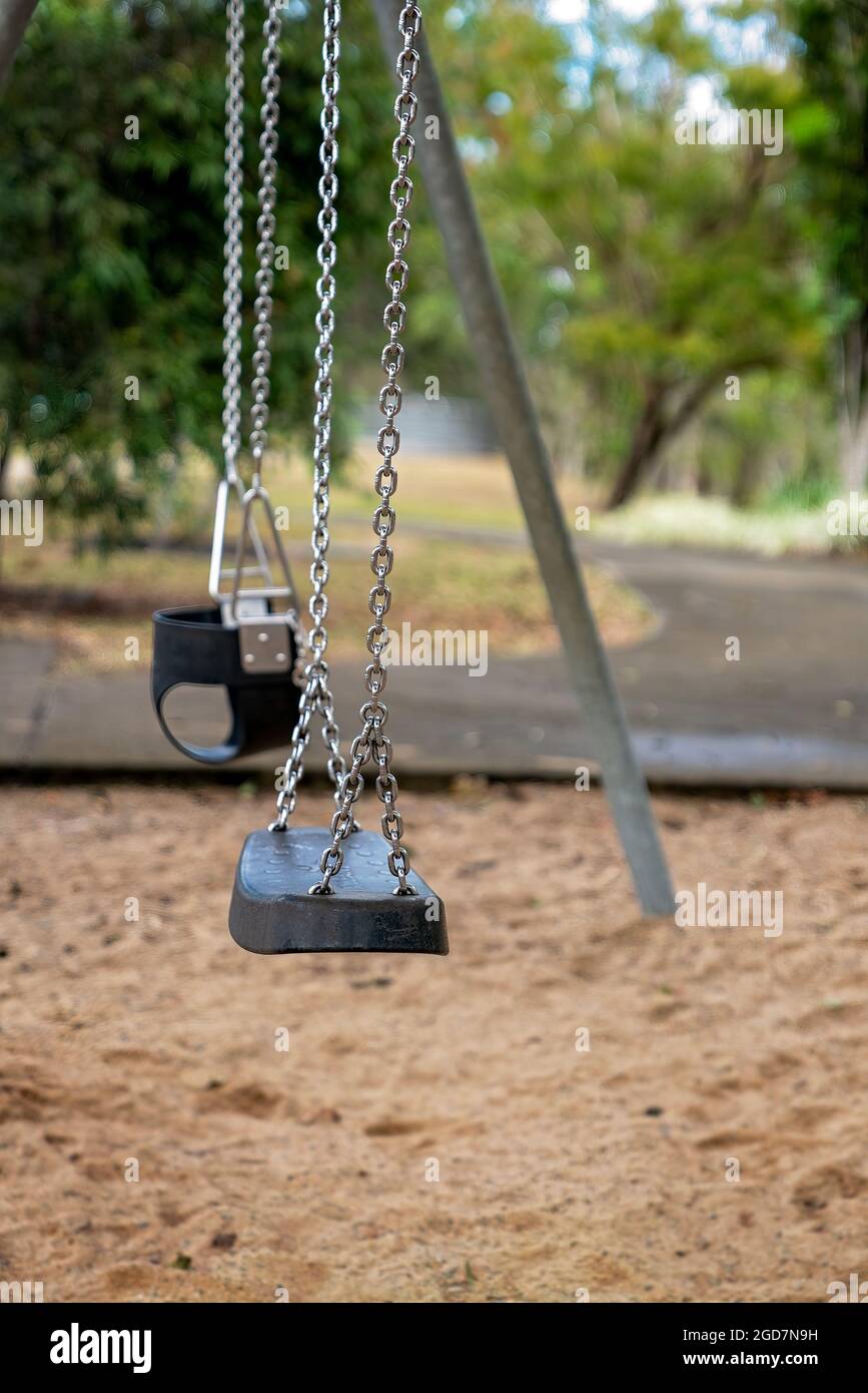 An empty swing set on a chain in an outdoor playground Stock Photo - Alamy