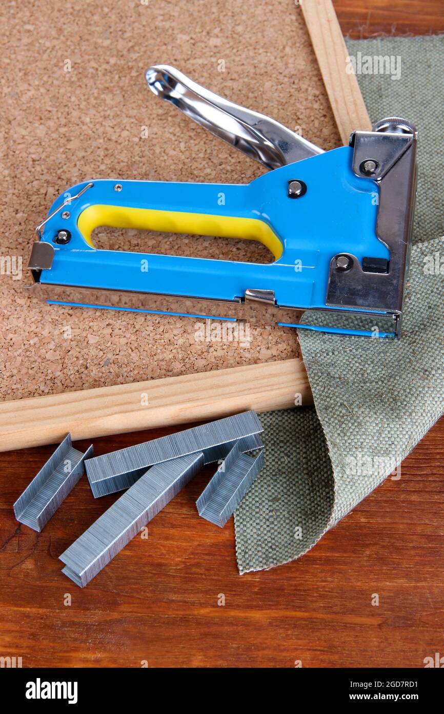 Construction stapler with staples and cork board on wooden background ...
