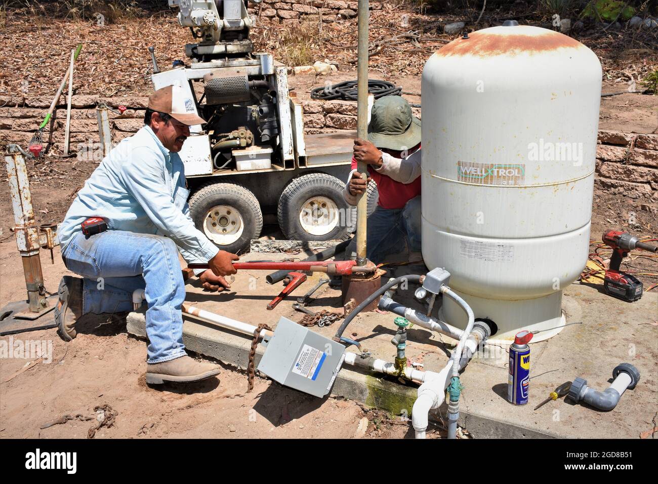 Two men pulling a water well pump and replacing the 20 foot pipe which ...