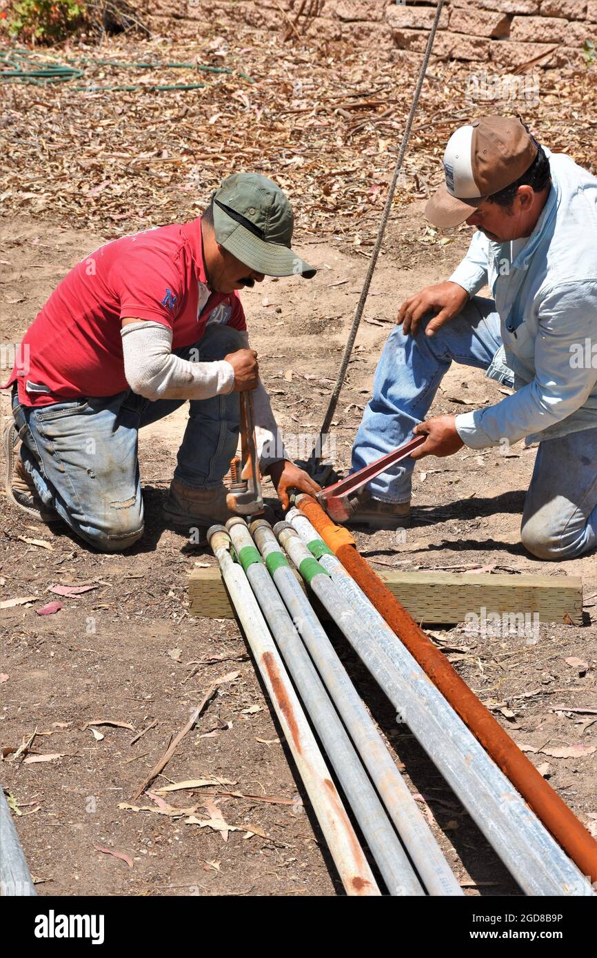 Two men pulling a water well pump and replacing the 20 foot pipe which ...