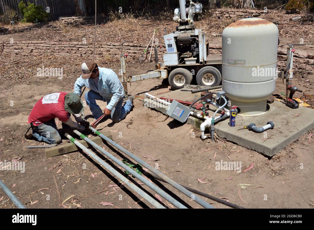 Two men pulling a water well pump and replacing the 20 foot pipe which ...