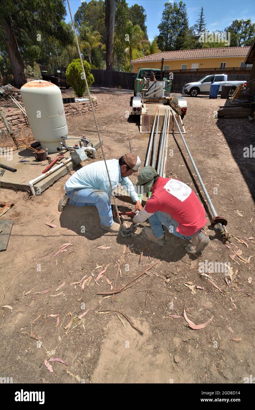 Two men pulling a water well pump and replacing the 20 foot pipe which ...