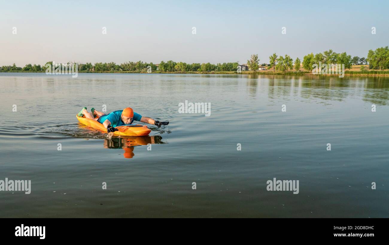 athletic, senior man is paddling a prone kayak on a lake in Colorado ...
