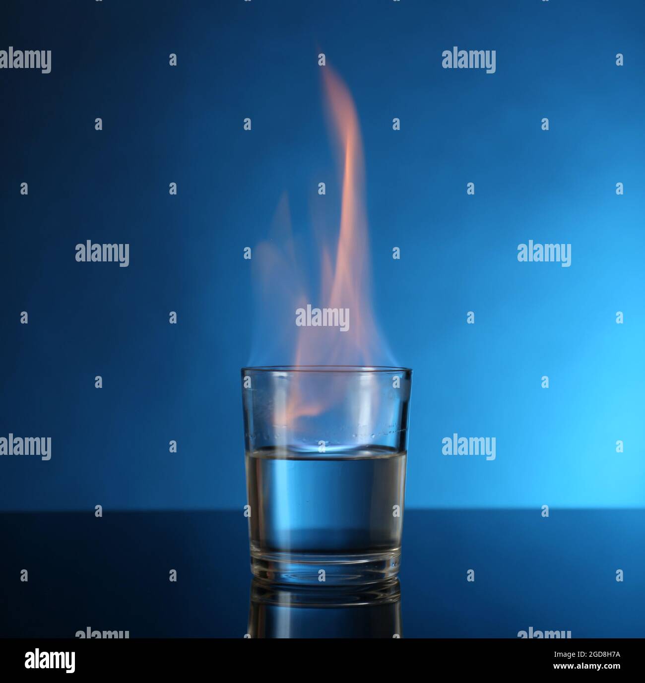 Glass with burning alcohol on blue background Stock Photo - Alamy