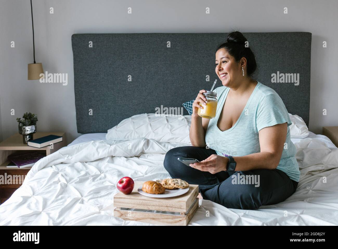 Curvy latin girl with smartphone having breakfast and drinking orange ...