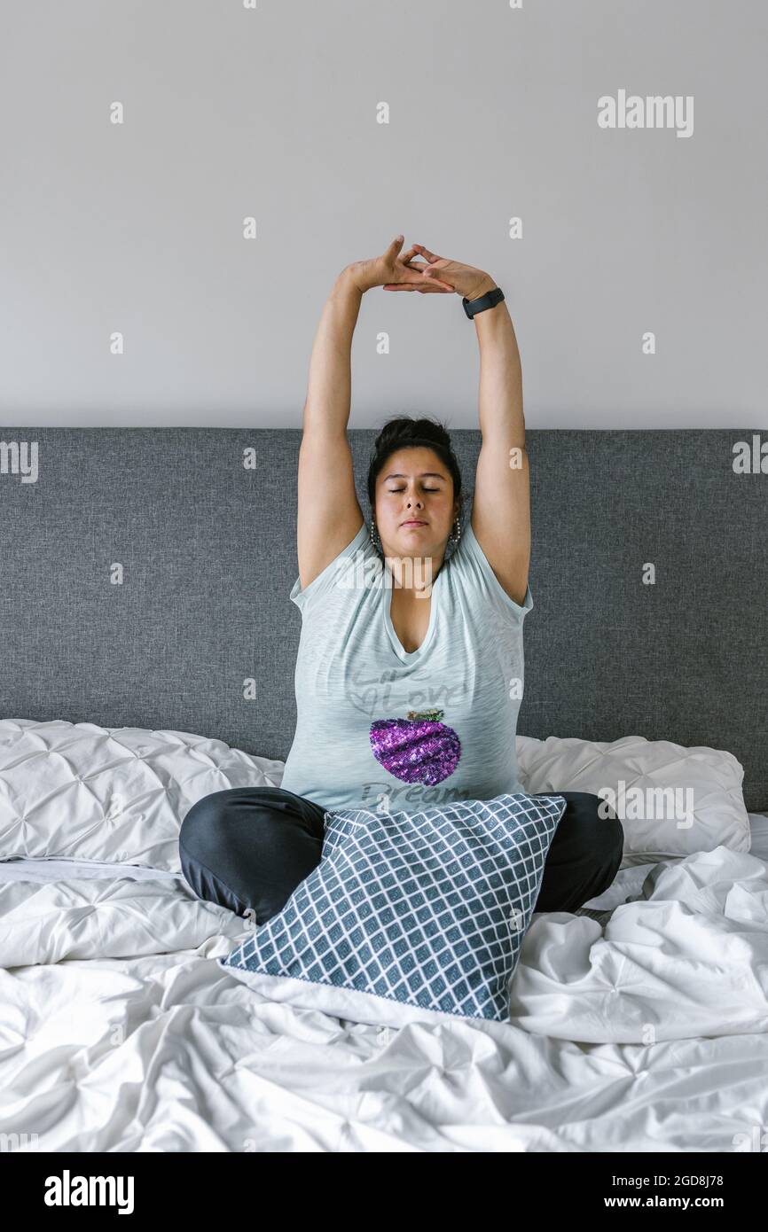 Plus size latin woman sitting on bed stretching arms up in Latin ...